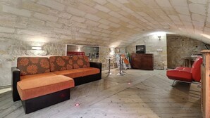 Um quarto com teto de pedra, um sofá, uma cadeira vermelha e uma área de refeições com cadeiras e mesas.