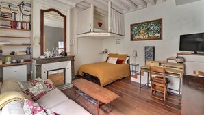 Quarto com cama, escrivaninha, cadeira, banco, lareira, estante e televisão.