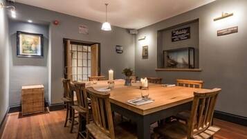 Uma sala de jantar com uma mesa e cadeiras de madeira, uma vela e obras de arte nas paredes.