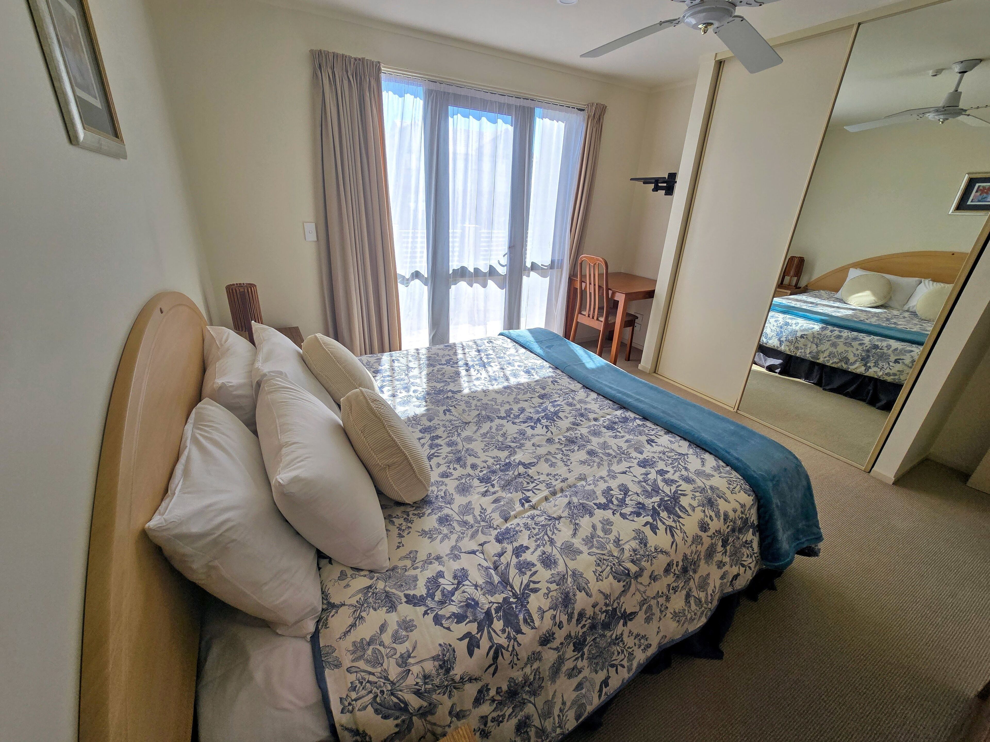 Um quarto com cama, cadeira, escrivaninha e ventilador de teto.