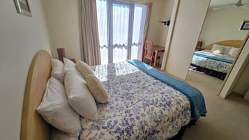 Um quarto com cama, cadeira, escrivaninha e ventilador de teto.