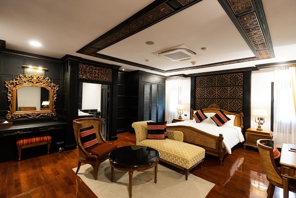 Um quarto espaçoso com uma cama grande, um espaço de estar com uma poltrona, uma escrivaninha e um espelho.