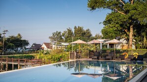 Piscina com espreguiçadeiras e guarda-sóis, cercada por vegetação e um deck de madeira.