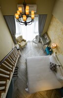 Quarto de hotel com cama, escrivaninha, cadeira, lustre e escada.