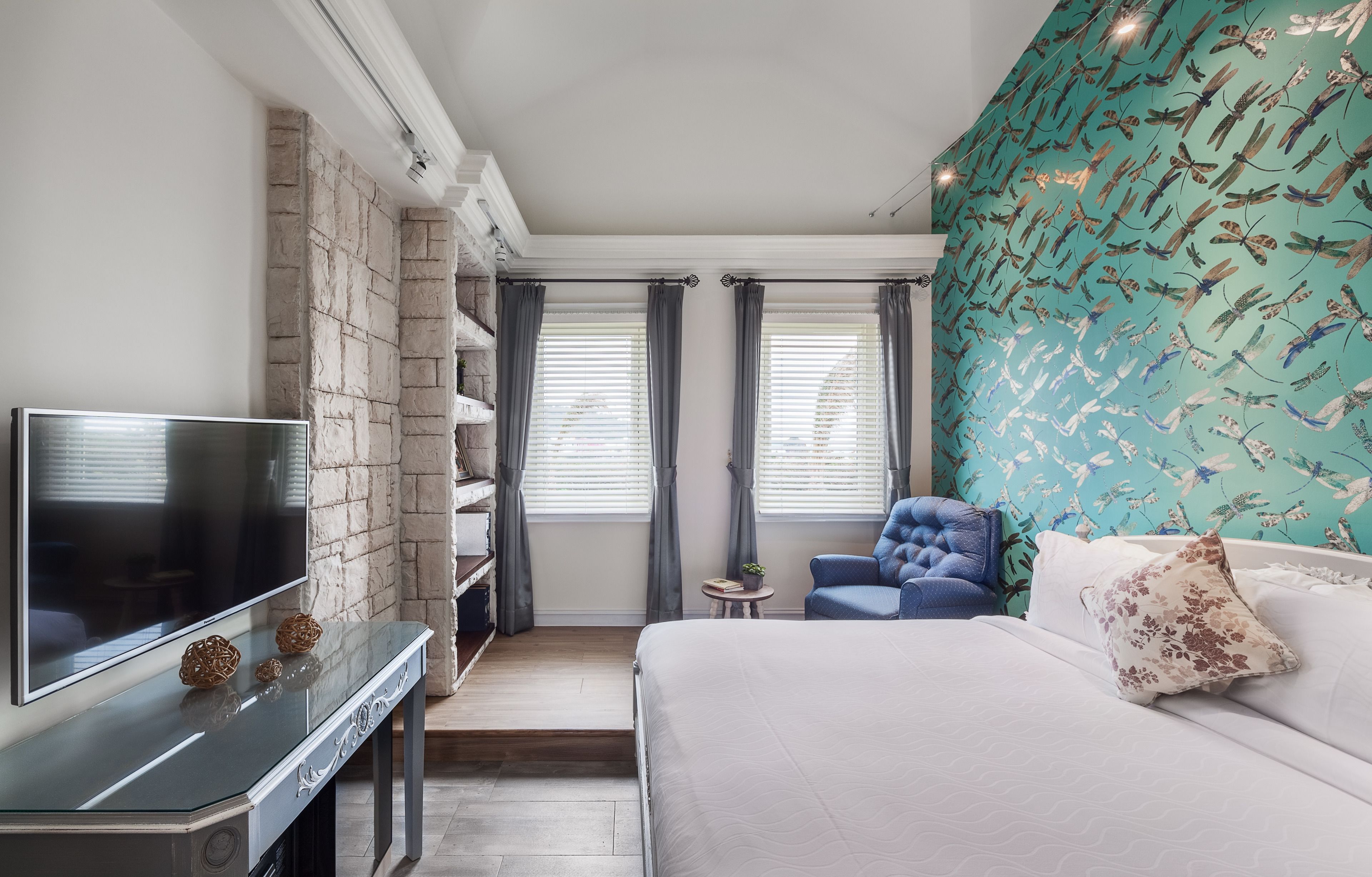 Um quarto com televisão, cama, poltrona azul e parede com padrão de libélula.