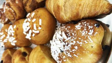 Diversos pastéis, incluindo croissants e pães, alguns cobertos com açúcar em pó e outros com sementes.