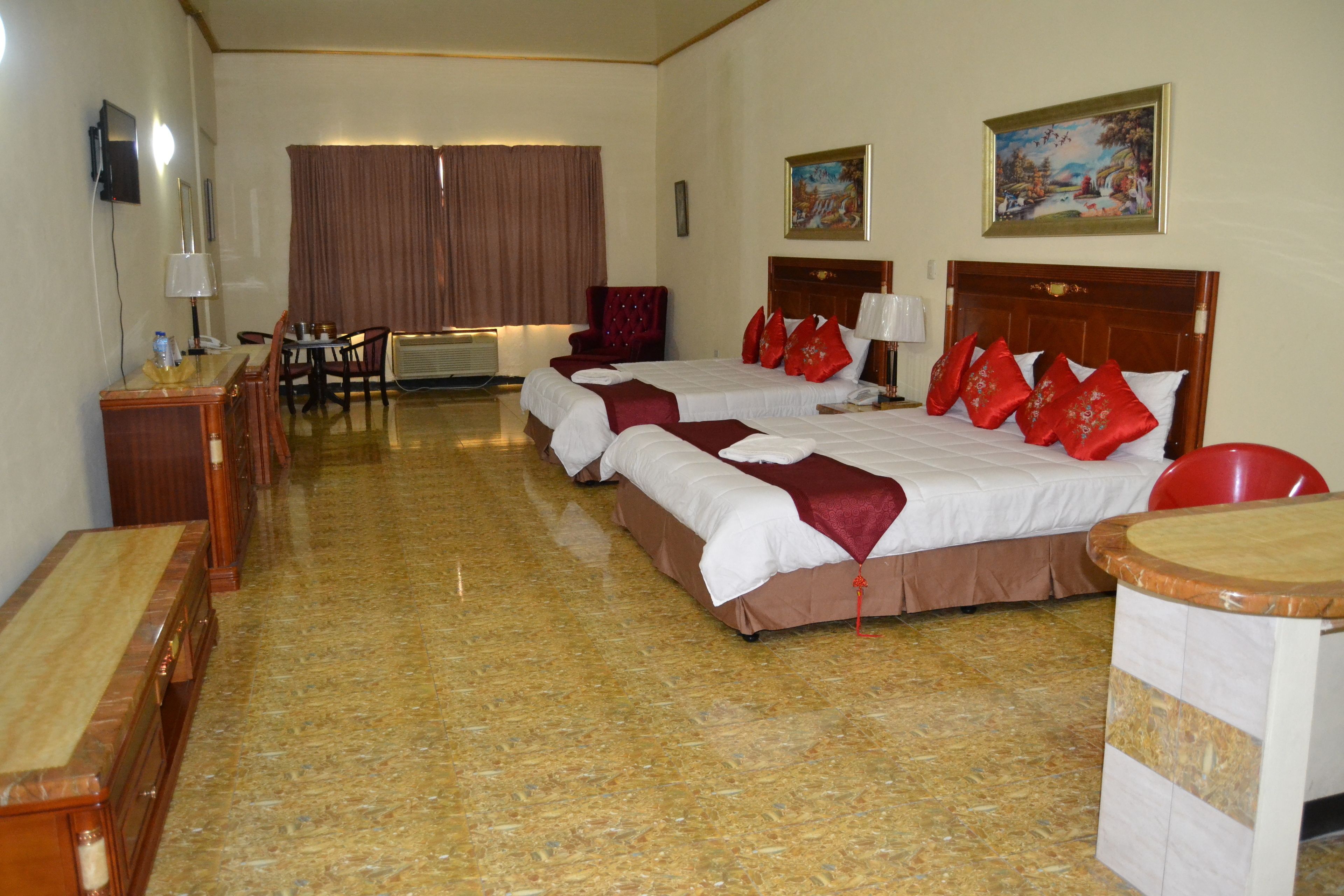 Quarto de hotel com duas camas, uma escrivaninha, uma cadeira e uma mesa de jantar.