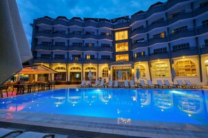 Um hotel com piscina, várias varandas e uma entrada bem iluminada.