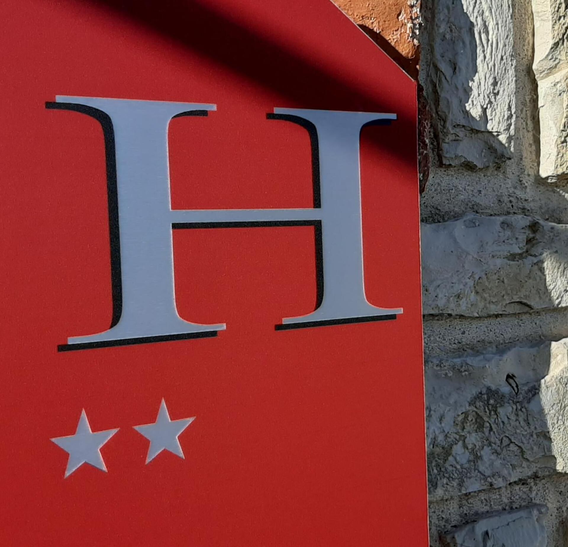 Um grande letreiro em formato de 'H' em destaque, com duas estrelas abaixo, fixado em um fundo vermelho.