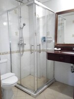 Box de chuveiro com paredes de vidro, vaso sanitário branco e bancada escura com espelho em cima.