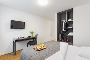 Quarto de hotel moderno com cama, escrivaninha com cadeira, televisão de tela plana, guarda-roupa e bandeja com itens de café da manhã.