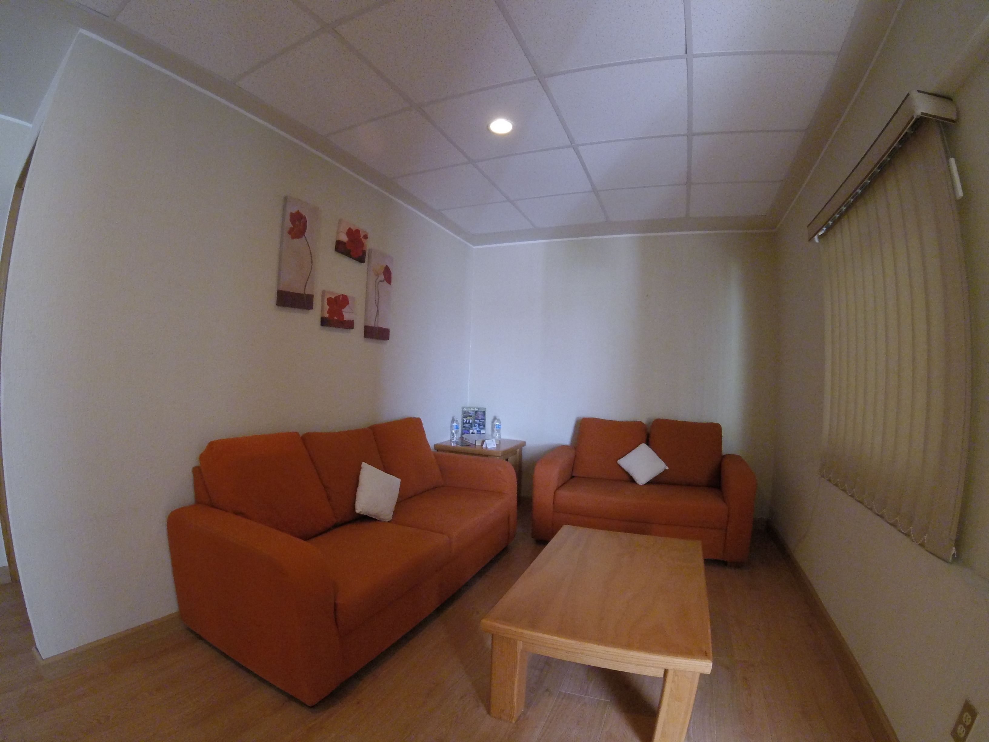 Quarto com dois sofás laranja, uma mesa de centro de madeira e uma mesinha lateral com uma garrafa de água.