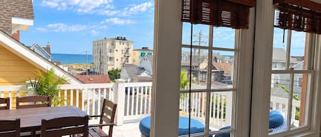 Uma varanda com mesa e cadeiras, uma cadeira de vime e vista para o oceano e edifícios.