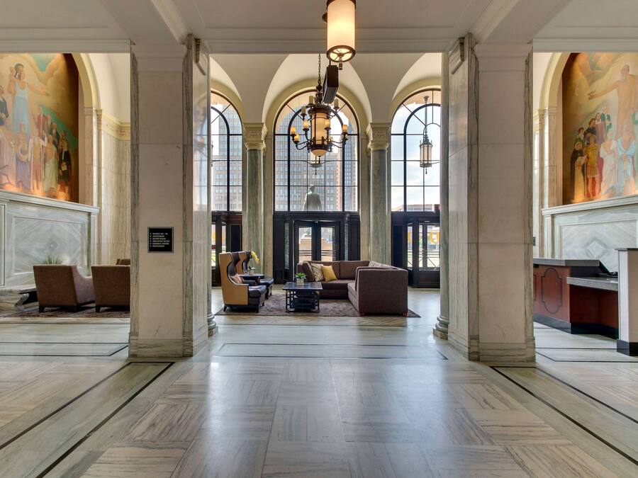 Um hall amplo com pisos de mármore, área de estar com sofás e poltronas, e janelas grandes com arcos.