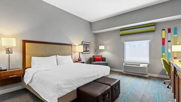 Quarto de hotel com uma cama grande, mesas de cabeceira, escrivaninha, cadeira, janela e aparelho de ar condicionado.