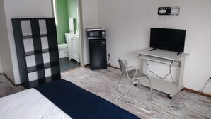 Quarto com cama, escrivaninha, televisão, micro-ondas e frigorífico.
