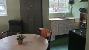 Uma cozinha compacta com pia, armários e fogão. Há uma mesa de jantar com cadeiras e um vaso de planta.