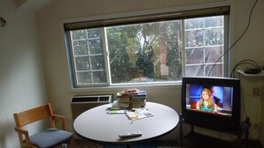 Um quarto com uma mesa redonda, uma televisão, uma janela e uma cadeira.