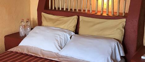 Uma cama com colcha listrada, duas almofadas e cabeceira com ripas verticais.