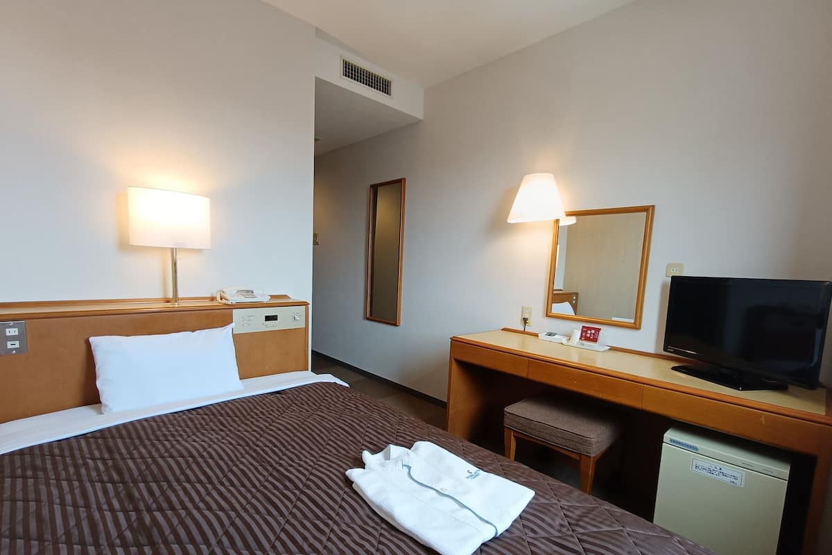 Quarto de hotel com uma cama, escrivaninha com televisão, espelho e um pequeno frigorífico.