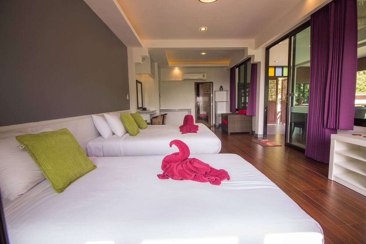 Quarto de hotel com duas camas, uma escrivaninha e porta de vidro deslizante para uma varanda.