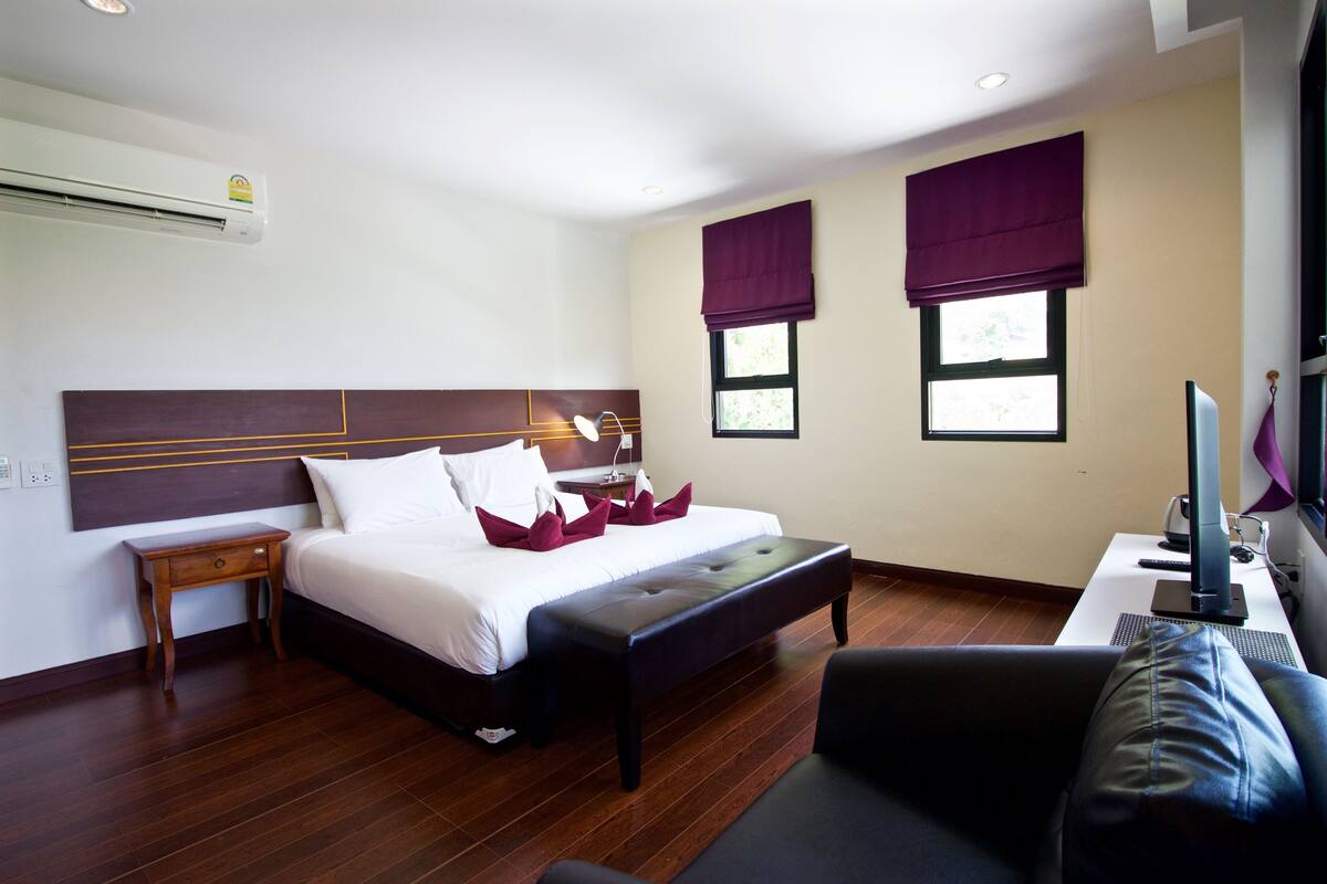 Quarto de hotel com cama, mesa de cabeceira, abajur e escrivaninha com computador.