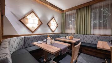Um restaurante acolhedor com mesas de madeira e bancos estofados, arandelas nas paredes e uma grande janela com cortinas leves.