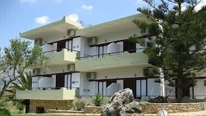 Um edifício com várias andares e varandas, cercado por vegetação e um muro de pedra.