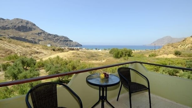 Varanda com mesa e cadeiras, vista para uma paisagem montanhosa e o mar.