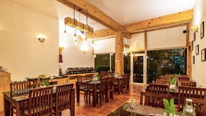 Uma sala de jantar com mesas e cadeiras de madeira, um balcão de bar e janelas amplas.