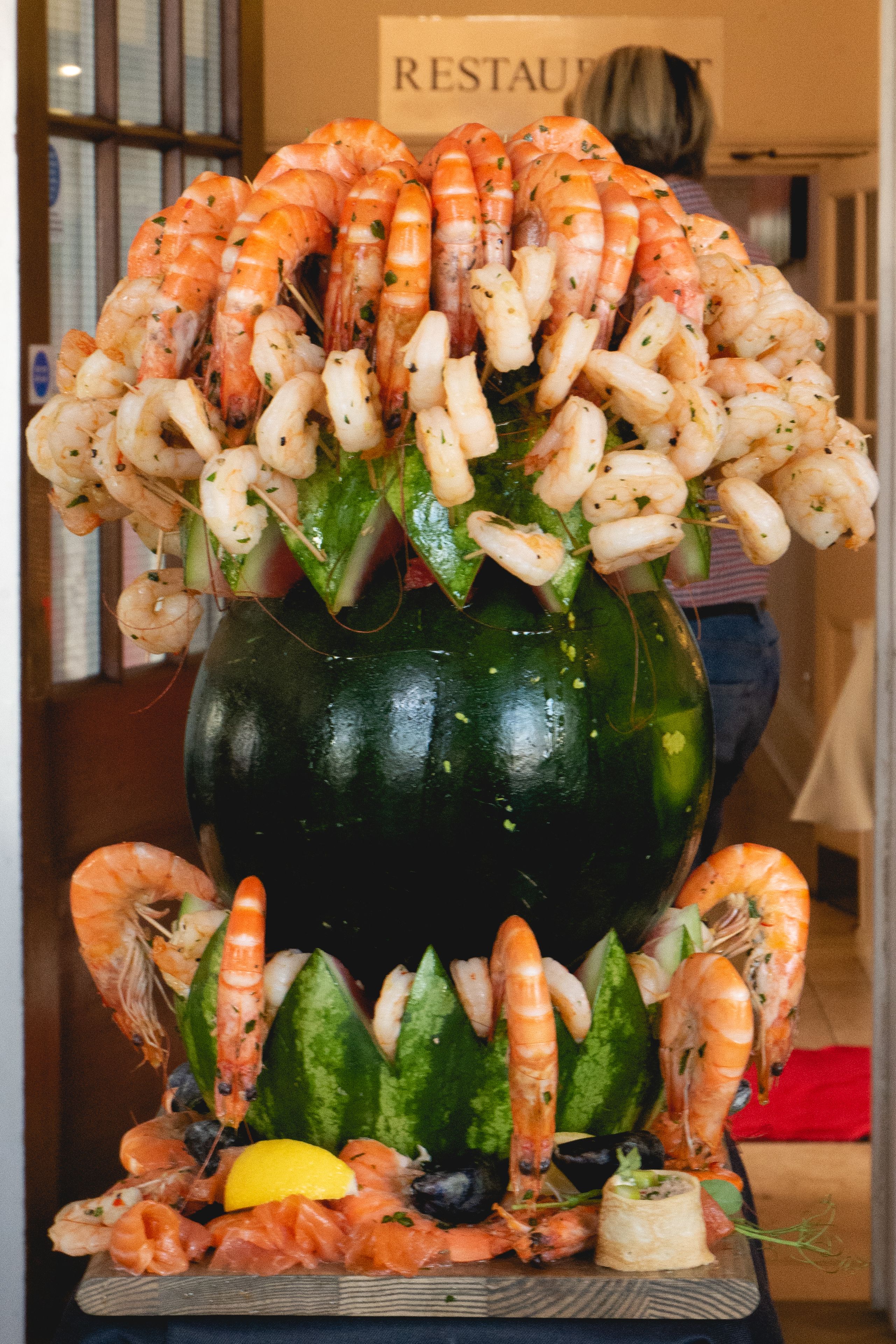 Um vaso decorativo grande cheio de diversos frutos do mar, incluindo camarão e lula, sobre uma mesa de madeira.