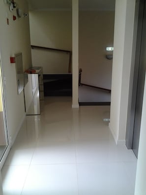Um corredor com cozinha à esquerda, escada no centro e porta à direita.