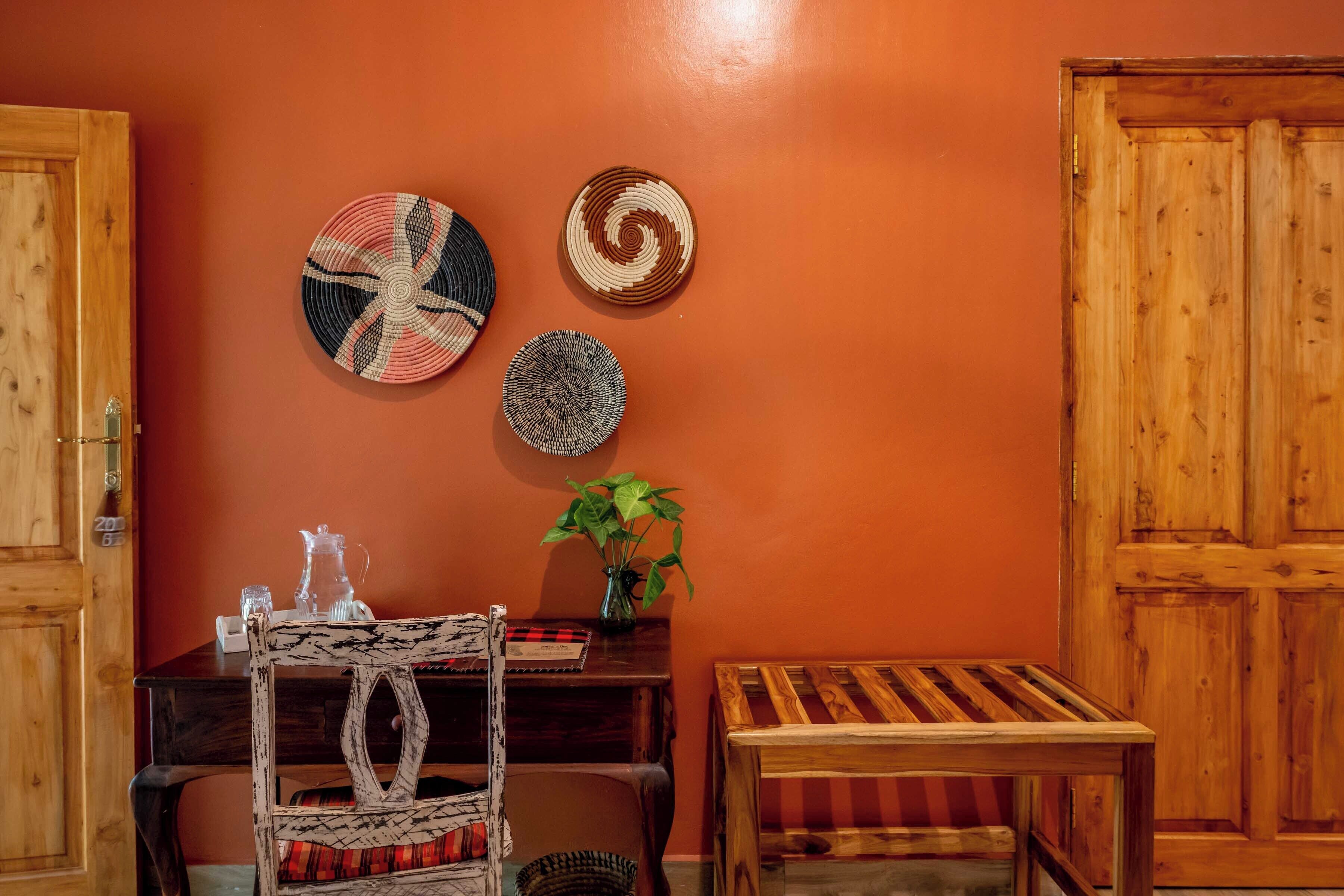 Quarto com porta de madeira, mesa com vaso e jarra, e três pratos decorativos pendurados na parede.