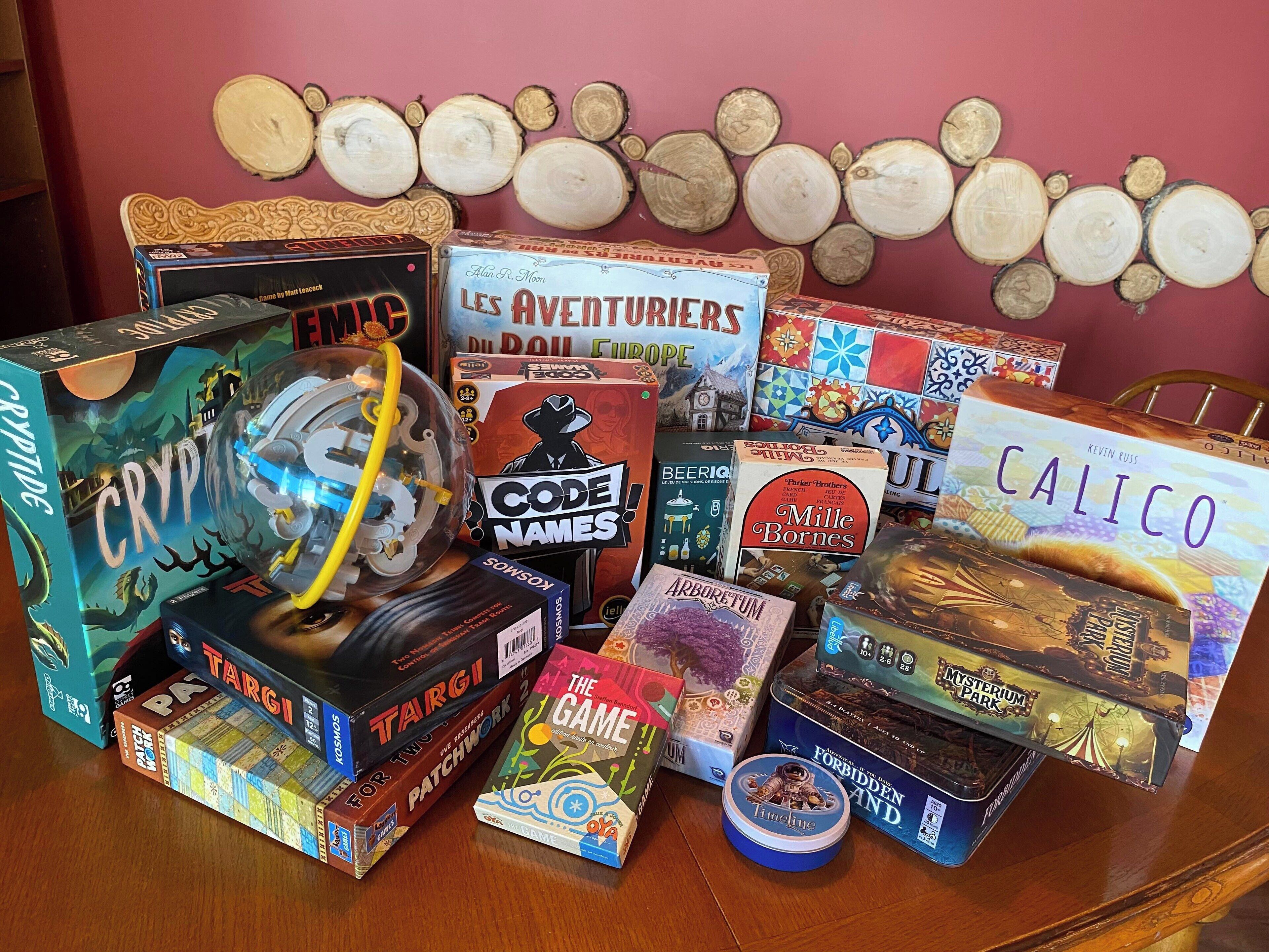 Diversos jogos de tabuleiro e um brinquedo sobre uma mesa de madeira.