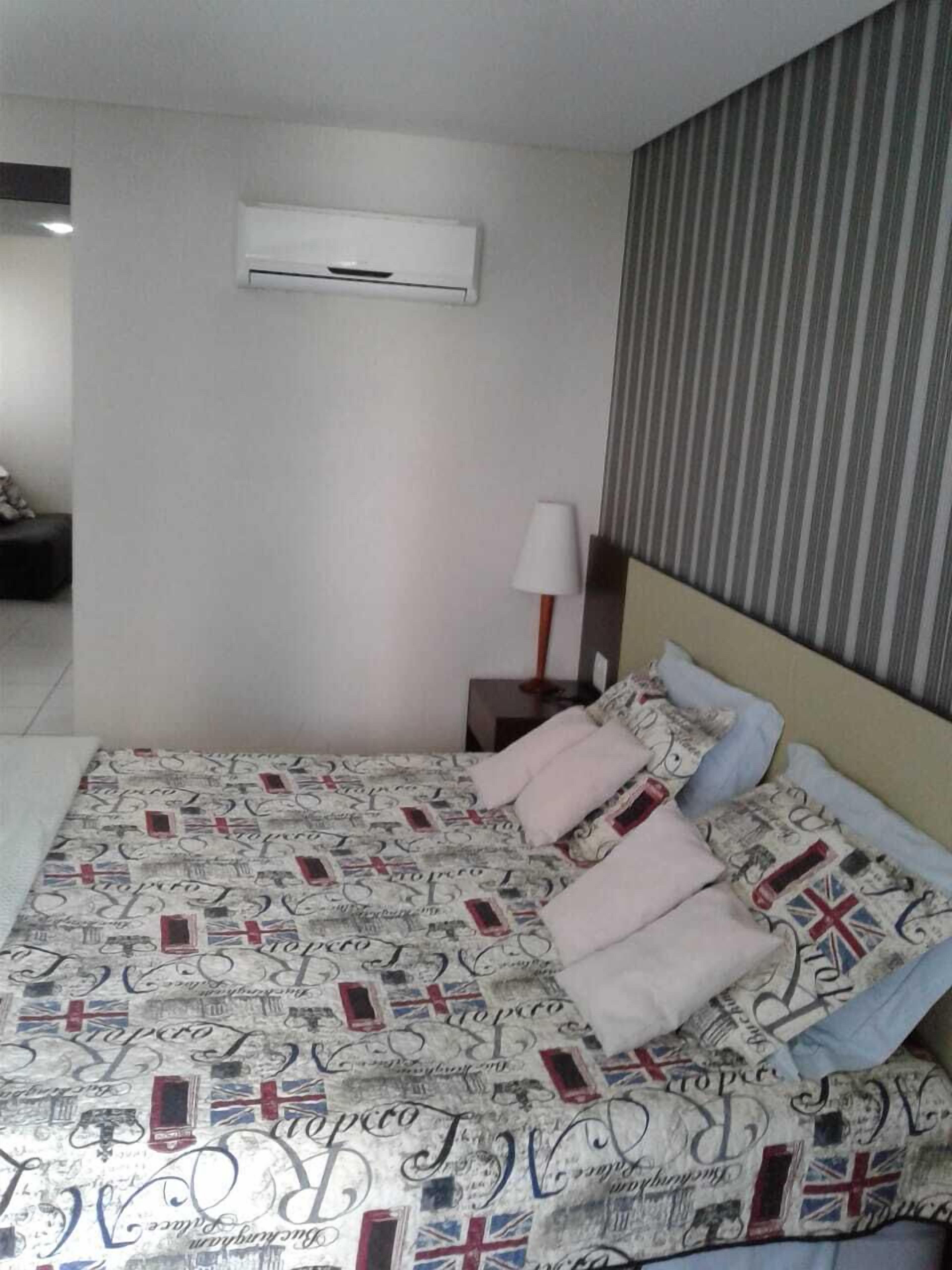 Quarto de hotel com uma cama, ar condicionado, uma luminária e parede listrada.