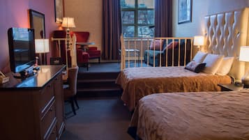 Quarto de hotel com uma cama, uma escrivaninha com televisão, uma cadeira, uma mesinha e uma janela com cortinas.