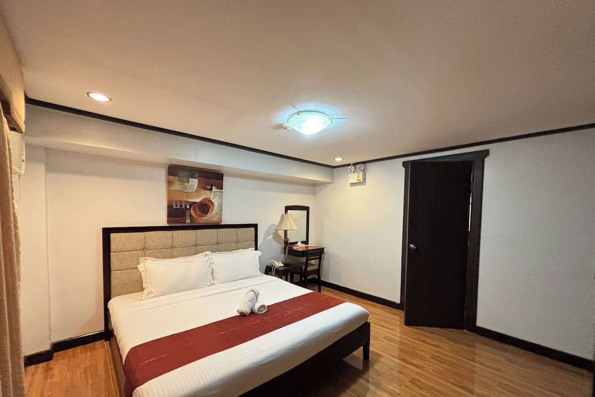 Quarto de hotel com uma cama grande, uma mesa de cabeceira, uma luminária e uma porta.
