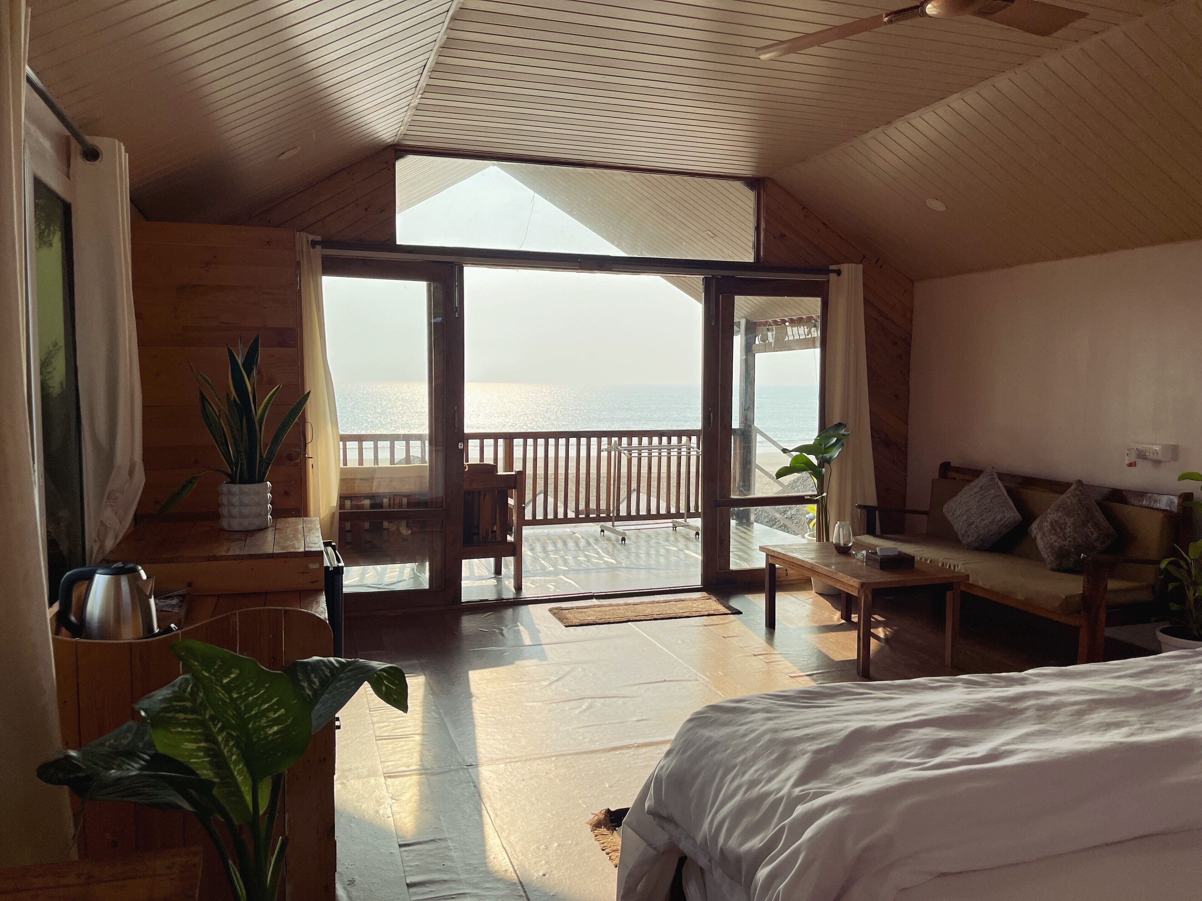 Quarto com uma cama grande, uma escrivaninha de madeira, uma cadeira, uma mesa e uma varanda com vista para o mar.