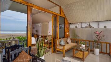 Ampla sala de estar com vista para a praia, móveis de madeira e plantas em vasos.