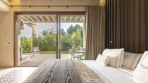 Quarto com uma cama grande, vista para um jardim e porta de vidro deslizante para uma área de estar externa.