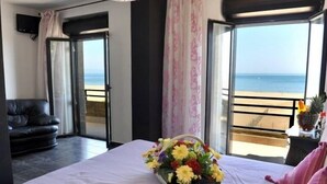 Quarto de hotel com cama, uma cadeira, janela com vista para a praia e um cesto de flores.