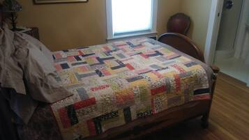 Quarto com cama de madeira, colcha, cadeira, janela e porta.