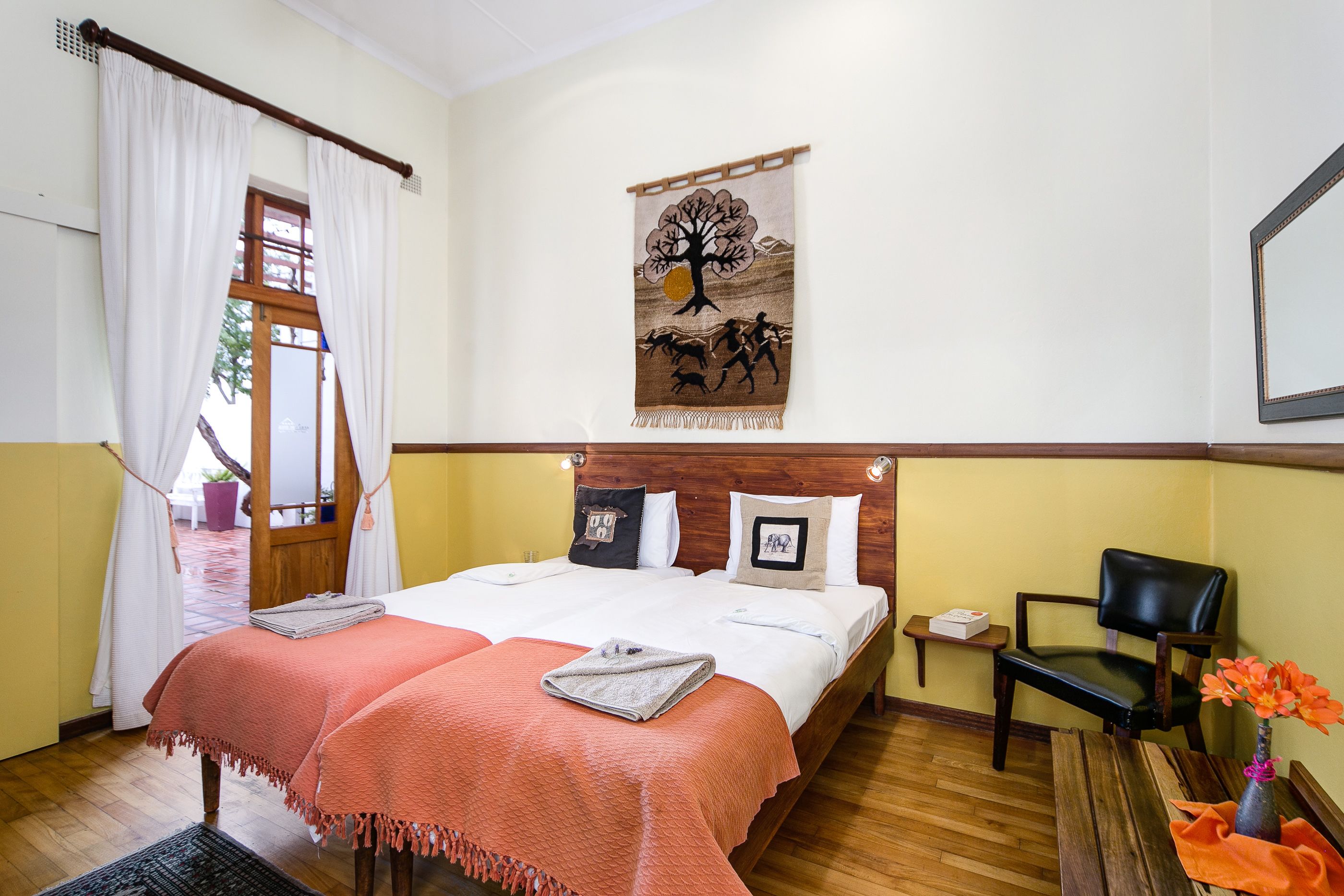 Um quarto com uma cama, uma cadeira, uma mesa, um tapeçário e uma janela com cortinas.