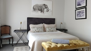 Quarto com cama grande, duas mesas de cabeceira, uma cadeira e uma pequena mesa com abajur.