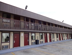 Um motel com vários quartos, cada um com um número na porta, um pequeno ar condicionado e uma varanda.