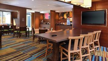 Uma sala de conferências de hotel com uma grande mesa, cadeiras, uma televisão e um canto para café.