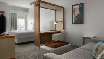 Quarto de hotel com cama, escrivaninha com cadeira, televisão e mesa pequena.