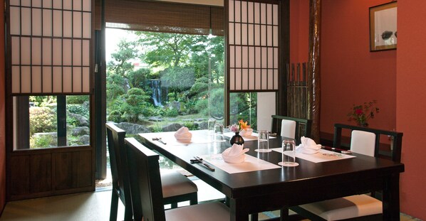 Uma área de refeições com vista para um jardim, mesa posta com guardanapos brancos e portas deslizantes japonesas tradicionais.