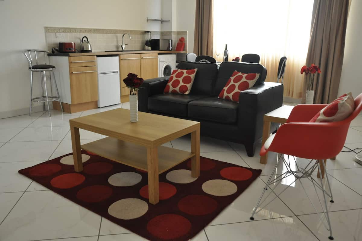 Uma sala de estar moderna com um sofá preto, almofadas com bolinhas vermelhas e brancas, uma mesa de centro de madeira e uma cadeira vermelha.