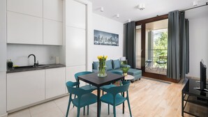 Cozinha moderna com armários brancos, bancada preta e área de refeições com cadeiras azul-turquesa e mesa.